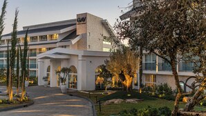 Um hotel moderno com um letreiro 'GAV' em destaque, um acesso arborizado e uma mistura de estilos arquitetônicos.