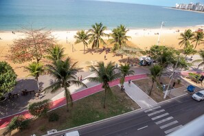 Vista à beira-mar com uma calçada, palmeiras e uma visão clara do oceano.