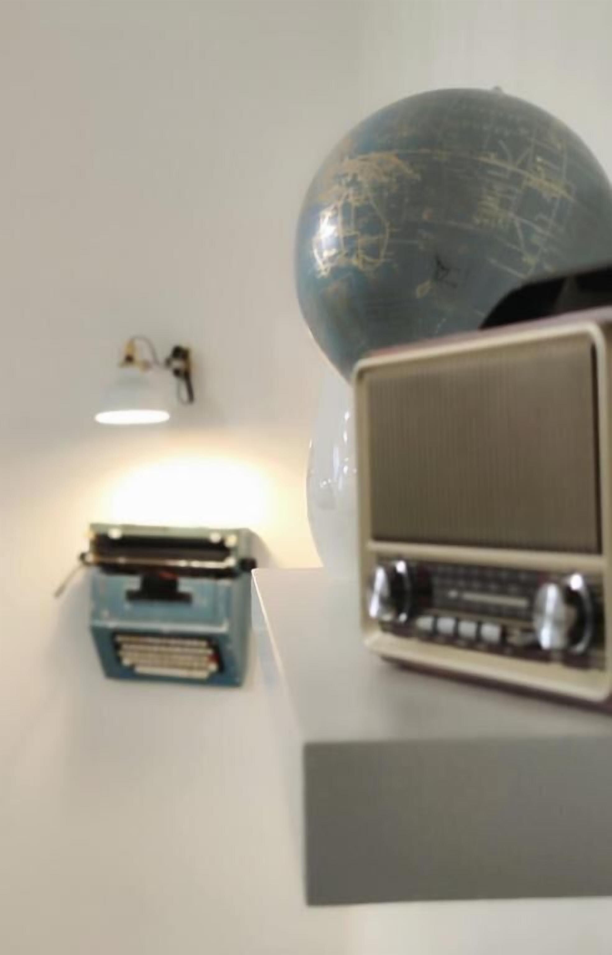 Um rádio antigo, um globo terrestre e um abajur sobre uma superfície branca.