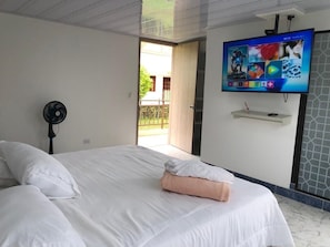 Quarto de hotel com cama, televisão na parede, ventilador e vista para o exterior.