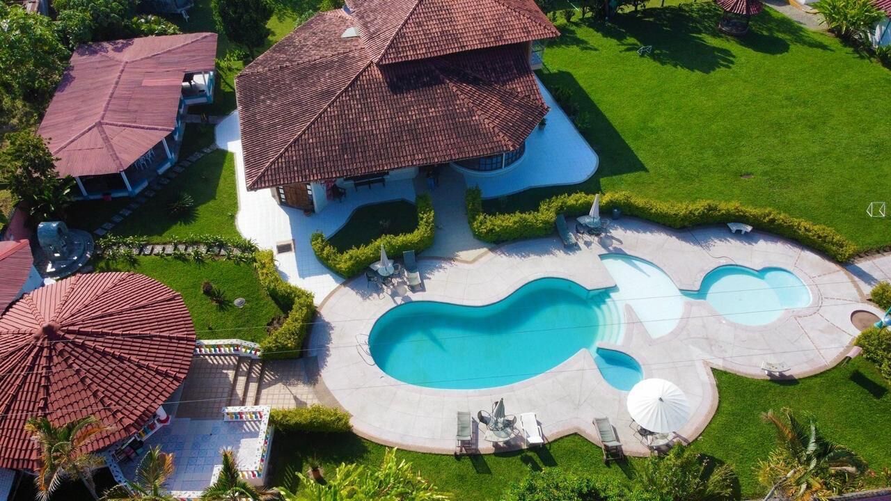 Um imóvel residencial com piscina, vários guarda-sóis e um gramado bem cuidado.