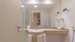 Uma casa de banho de hotel com lavatório, espelho, porta-toalhas e secador de cabelo.