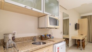 Uma cozinha de hotel compacta, com micro-ondas, pia e pequena geladeira.