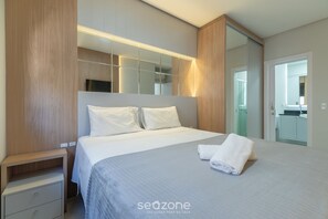 Quarto de hotel moderno com uma cama grande, mesa de cabeceira, espelho e guarda-roupa.
