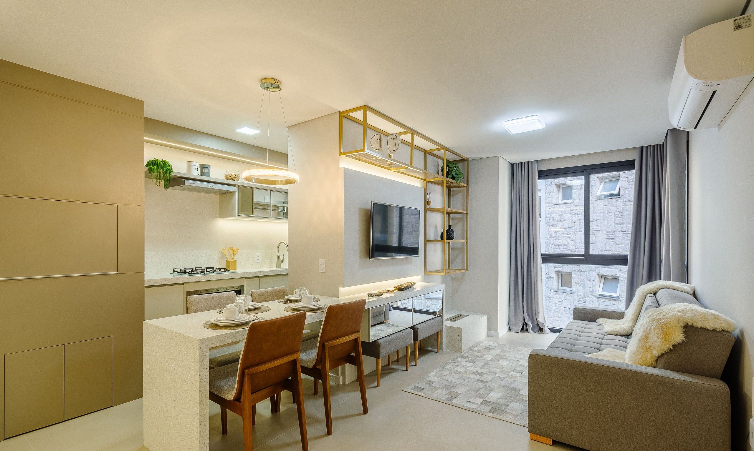 Uma sala moderna com sofá, área de jantar com mesa e cadeiras, e cozinha com forno embutido e televisão.