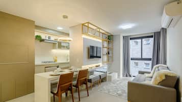 Uma sala moderna com sofá, área de jantar com mesa e cadeiras, e cozinha com forno embutido e televisão.