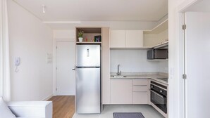 Uma cozinha compacta com geladeira de aço inoxidável, micro-ondas e forno embutido.