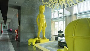Um lobby moderno com uma grande estátua amarela, um candelabro e uma área de estar.