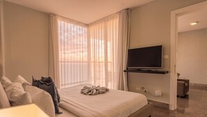Quarto de hotel com uma cama, televisão fixada na parede e vista para o exterior pela janela.
