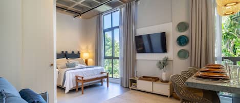 Quarto moderno com cama, mesa de cabeceira, televisão e área de refeições com cadeiras e mesa.