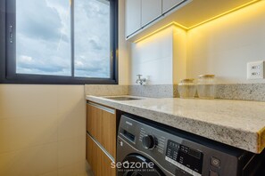 Cozinha moderna com máquina de lavar e secar integradas, bancada de granito e janela com vista para o céu.