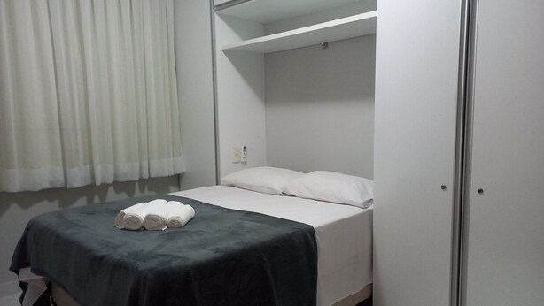 Um quarto com cama, mesa de cabeceira, espelho e guarda-roupa.