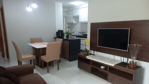 Uma sala de estar com sofá, mesa de jantar e cadeiras, cozinha e televisão sobre um móvel de madeira.