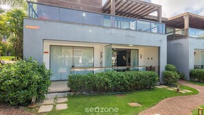 Um edifício moderno com fachada de vidro, área externa coberta e um jardim bem cuidado.