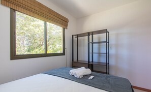 Quarto com cama, janela com persianas, guarda-roupa e mesa de cabeceira com controle remoto.