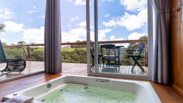 Uma banheira de hidromassagem em um deck de madeira, com vista para uma paisagem verde e um céu claro.