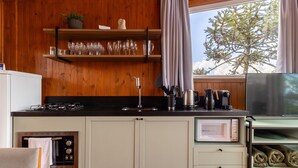 Uma cozinha compacta com painéis de madeira, micro-ondas embutido, chaleira e máquina de café.
