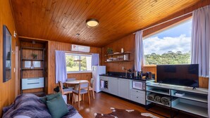 Interior acolhedor de uma cabana, com área de jantar, cozinha compacta e uma grande janela com vista panorâmica.
