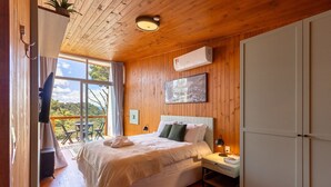 Quarto com cama, mesa de cabeceira e janela com vista para árvores.