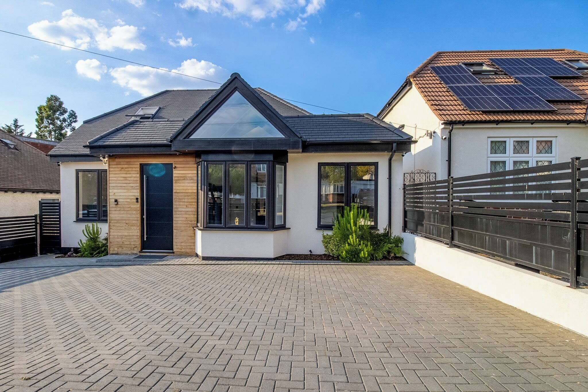 Uma casa moderna com telhado inclinado, painéis solares e uma entrada pavimentada.