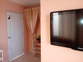 Quarto com porta fechada, cortina, escada e televisão na parede.