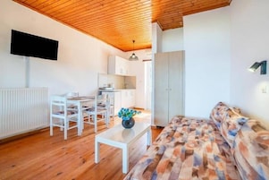 Uma sala de estar moderna com teto de madeira, um sofá, uma mesa de jantar com cadeiras e uma área de cozinha ao fundo.