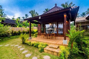 Um gazebo de madeira com telhado de azulejos, cercado por vegetação exuberante e palmeiras.
