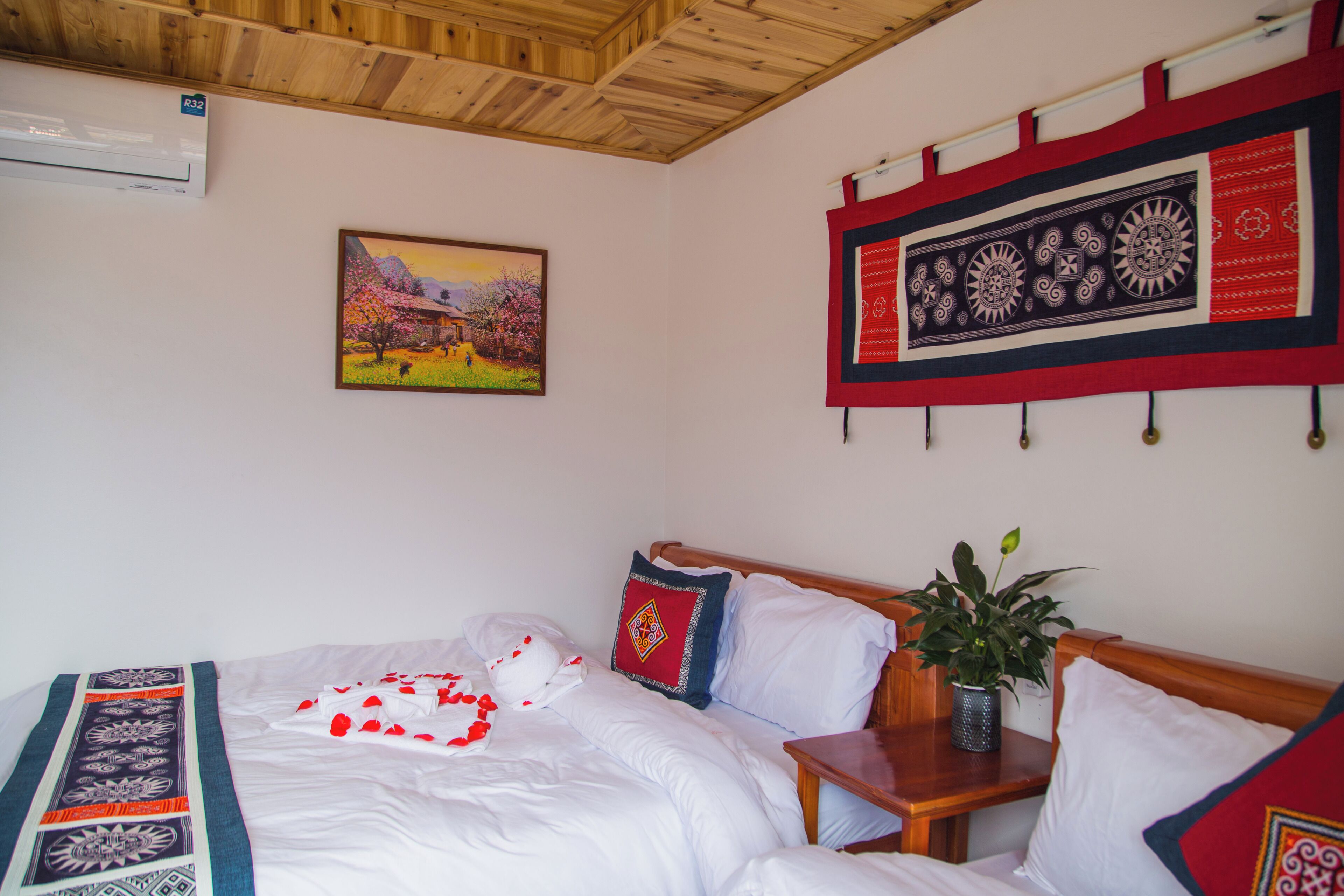 Quarto com teto de madeira, cama com roupa de cama branca, pintura, tapeçaria decorativa e planta em vaso.