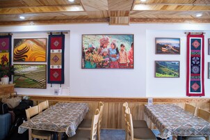 Quarto com teto e paredes de madeira, com área de refeições com mesas cobertas por toalhas estampadas, obras de arte nas paredes e um código QR para o cardápio de café da manhã.