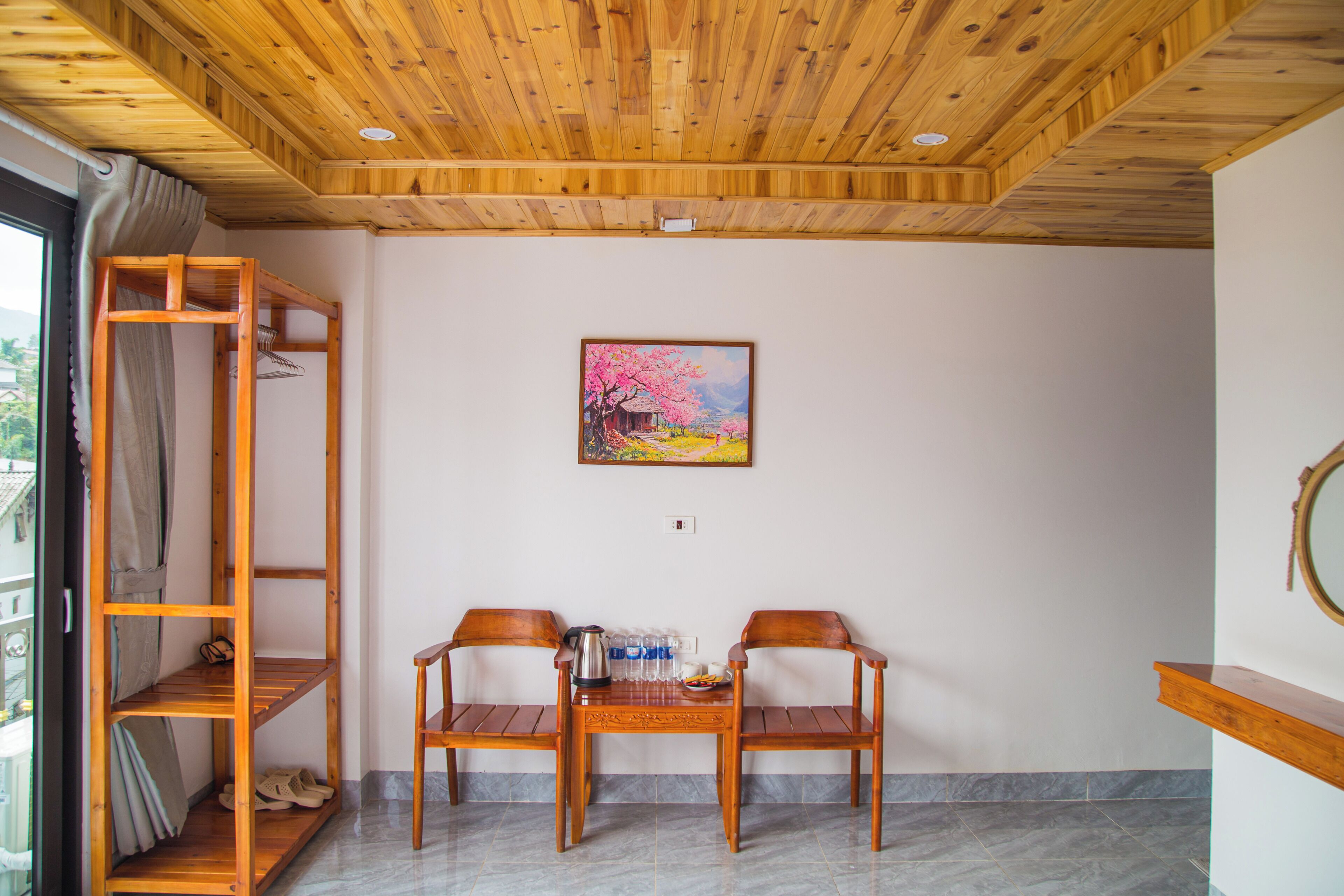 Quarto com teto de madeira, pintura de flores de cerejeira, cadeira de madeira, mesa com chaleira e prateleira com sapatos.