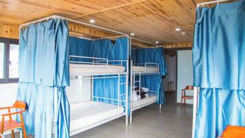 Quarto com beliche, cortinas azuis, teto de madeira e chão de azulejos.