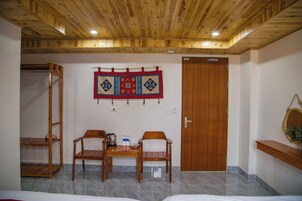 Quarto de hotel com teto e porta de madeira, uma cama, uma mesa com cadeiras e um tapeçário fixado na parede.