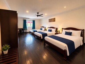 Quarto de hotel com duas camas, um ventilador de teto e janela com cortinas.
