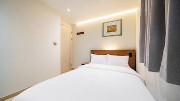 Quarto de hotel com cama, mesa de cabeceira, luminária na parede, porta e quadro emoldurado.