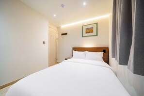 Quarto de hotel com cama, mesa de cabeceira, luminária na parede, porta e quadro emoldurado.