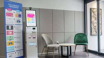 Quiosque com interface de tela sensível ao toque, uma cadeira, uma mesa e um painel decorativo na parede.