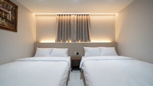 A hotel room with two beds, a painting on the wall, and a window with curtains.