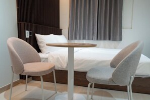 Quarto de hotel com uma cama, duas cadeiras, uma mesa redonda pequena e um painel de parede de madeira.