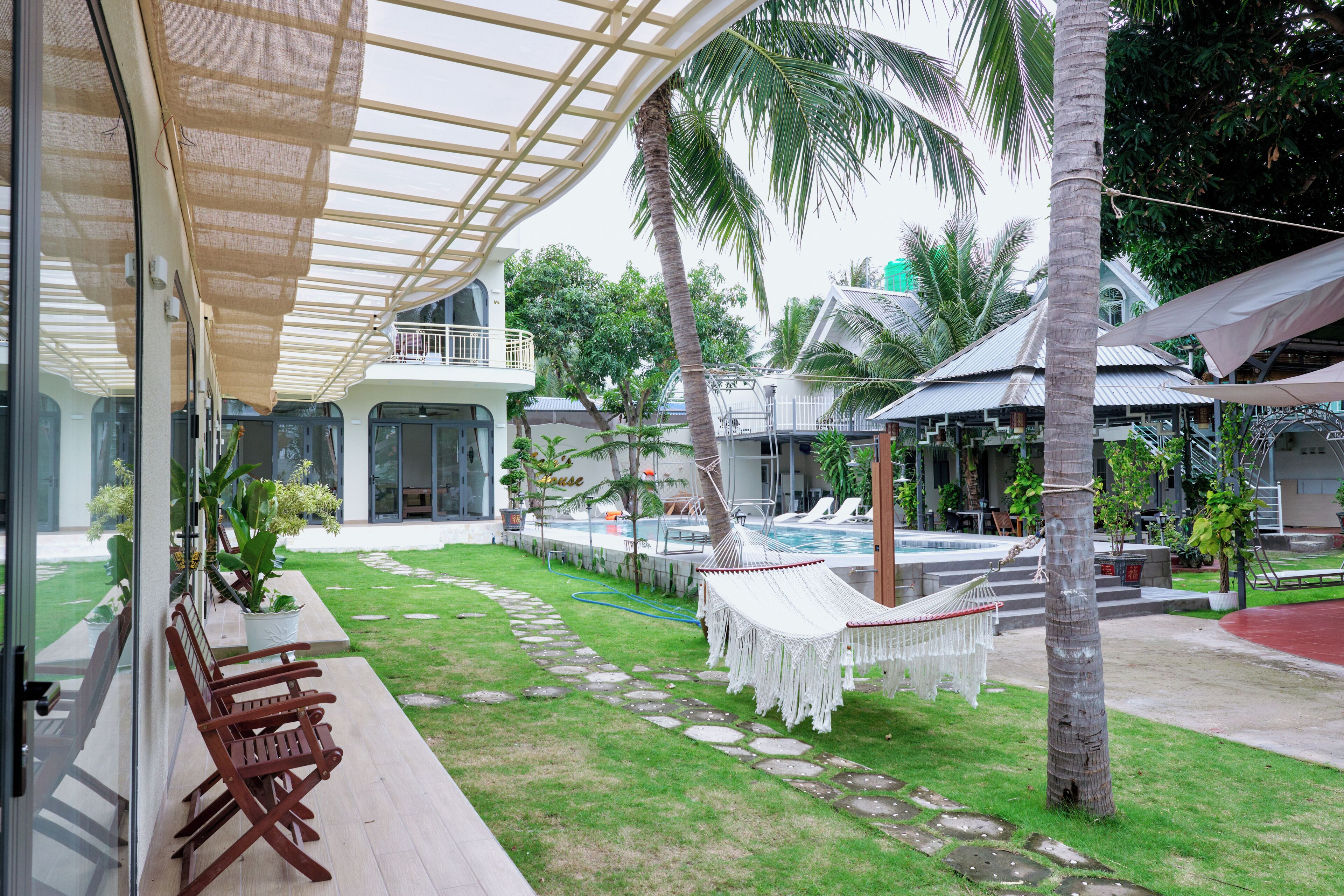 Uma área de piscina com rede, palmeiras e um espaço coberto para relaxar.
