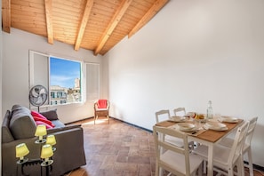 Quarto com mesa de jantar posta para quatro, um sofá, uma cadeira e janela com vista para edifícios.