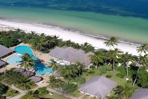 Vista aérea de um resort com piscina, praia e palmeiras.