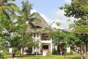 Um edifício de dois andares com telhado de palha, cercado por vegetação exuberante e palmeiras.
