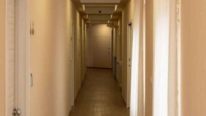Corredor de hotel com portas em ambos os lados, piso de madeira e teto com iluminação embutida.