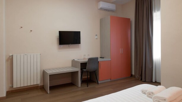 A hotel room with a bed, a desk, a chair, a television, a wardrobe, and a radiator.