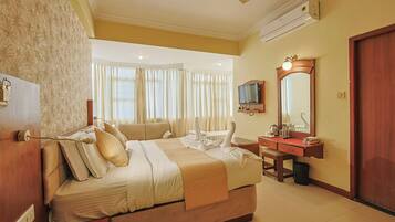 Quarto de hotel com cama, escrivaninha, espelho, televisão e ar condicionado.