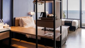 Quarto de hotel com uma cama de solteiro, uma escrivaninha com abajur e vista para o mar.