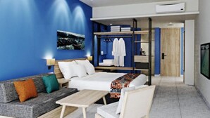 Quarto de hotel moderno com uma cama, sofá e uma pequena mesa. Há um guarda-roupa com roupas penduradas e uma televisão na parede.