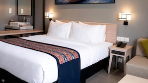 Quarto de hotel com cama, mesas de cabeceira, escrivaninha, cadeira, um quadro na parede e espelho.