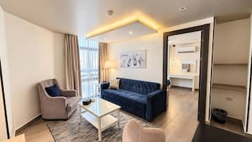 Quarto de hotel moderno com sofá, poltronas, mesa de centro e um quadro na parede.
