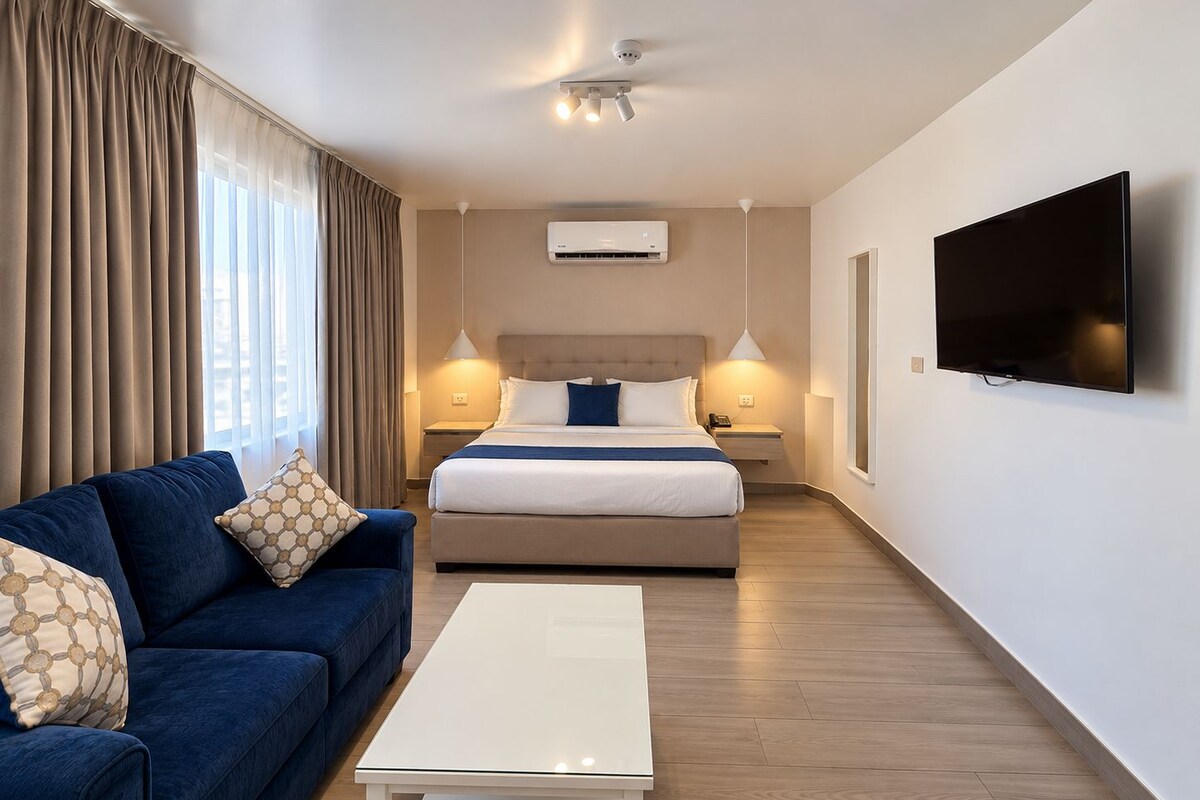 Quarto de hotel com cama, sofá, televisão e ar condicionado.